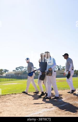 Diverse male teammates walking across pitching mound on baseball field ...