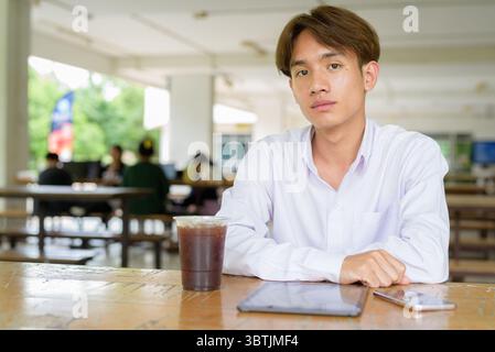 Non binary Asian university student in college campus using computer ...