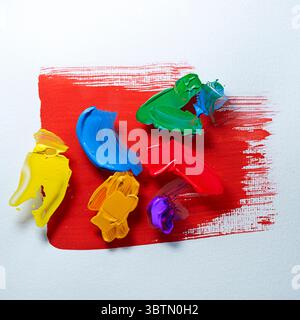 Assorted multi coloured paint blobs on a piece of glass over a brush ...