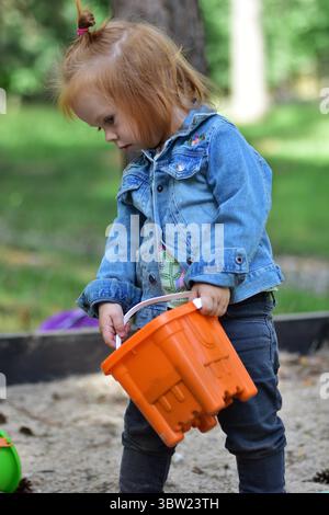 A red-haired girl in a denim shirt stands in profile with head bowed ...