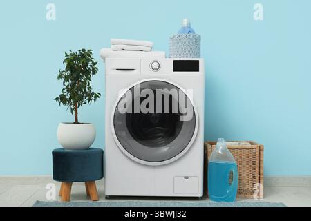 Modern washing machine, detergents, houseplant and clothes near light green wall indoors Stock ...