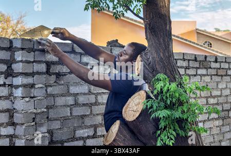 african bricklayer with a trowel ,building a surrounding bricks wall ...