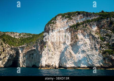 Majestic coastal cliffs with caves and lush greenery under a clear blue ...