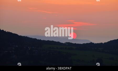 Golden sunrise above a hilly landscape with fog in the valley, cloudy ...