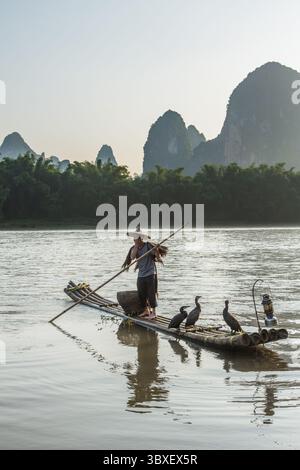 A cormorant fisherman poles his bamboo raft on the Li River iat sunset ...