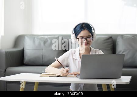 Teenage student wearing headphones writing study notes at home Stock ...