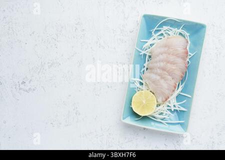 Sashimi from slices of raw white fish fillet on a blue plate on a white ...