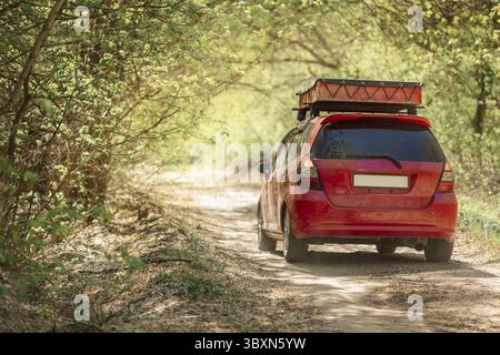 Red car drives along forest road on sunny spring day. View of ...