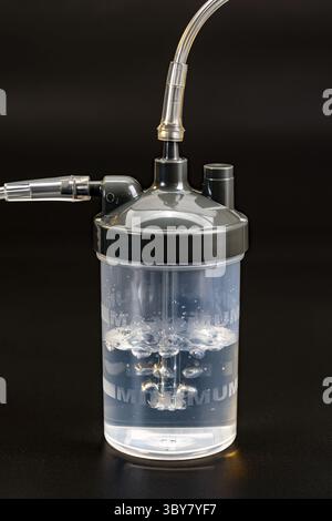 A medical oxygen humidifier bottle with attached tubing on black ...