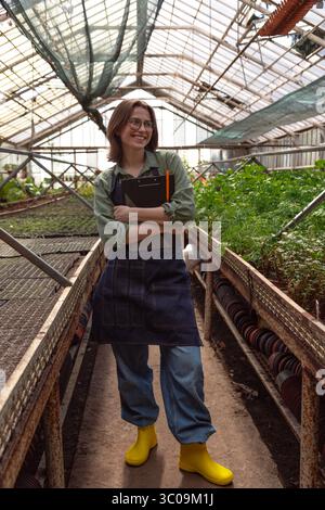 young female gardener in apron carrying tray with green succulent ...