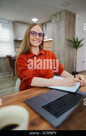 Focused Young Woman Writing In Notebook At Home Office With Laptop ...