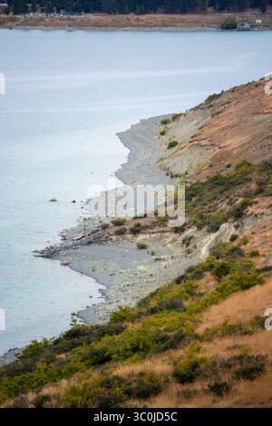 A serene landscape with a rocky shoreline, patches of snow, and distant ...
