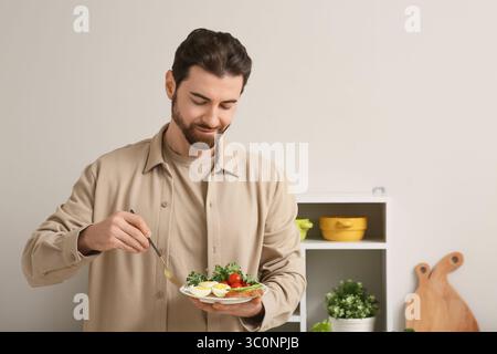 Handsome man eating boiled eggs, toast with avocado and vegetables in ...