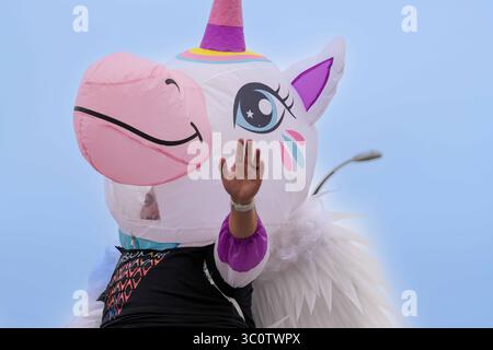 A person in an oversized inflatable unicorn costume waves cheerfully ...
