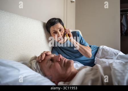 Distressed wife measuring fever while call doctor for ill senior ...