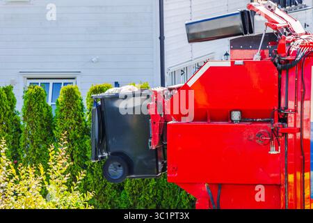 Black trash bin lifted by automated system of red blue garbage truck ...