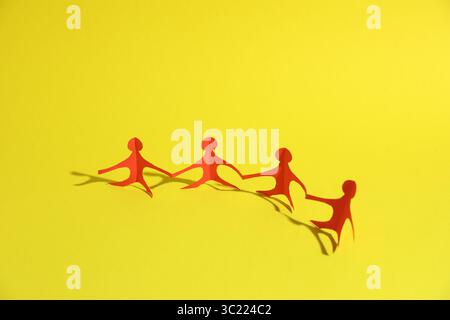 Human paper figures holding hands on yellow background. Space for text ...