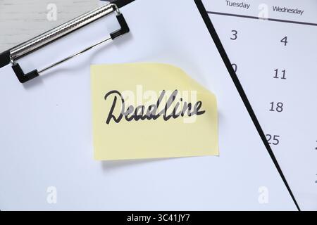 Sticky note with word Deadline and clipboard on white wooden table, top ...