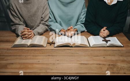 Group of Christians sit together and pray around a wooden table with ...
