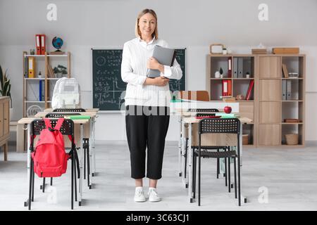Mature female math teacher with notebooks in classroom Stock Photo - Alamy