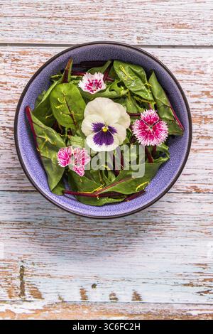 Bowl with edible flowers and herbs on a wooden table Stock Photo - Alamy