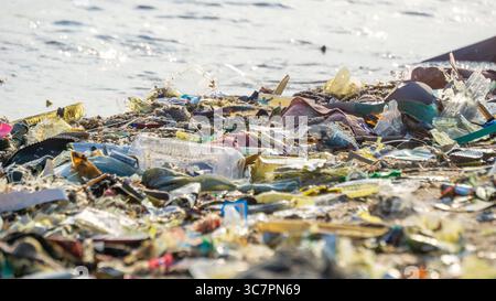 Various plastic waste scattered on the beach. Garbage pollutes and ...