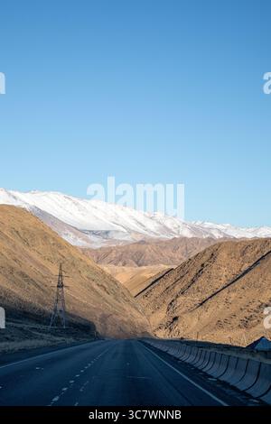 A vertical shot of an asphalt road through plants and rocky mountains ...
