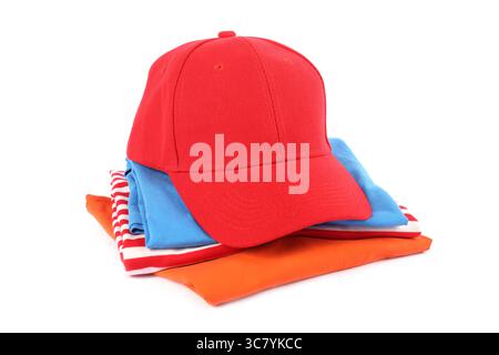 Red baseball cap and stack of folded t-shirts isolated on white. Mockup ...