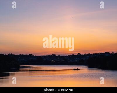A serene sunset casts vibrant orange and pink hues over a calm lake ...