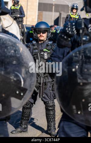 A police officer holding his baton stands at the ready outside the ...