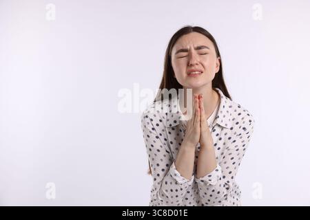 Emotional woman with clasped hands apologizing on white background ...