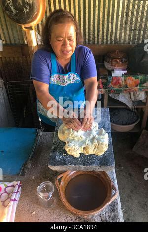 A vertical of a Hispanic woman kneading corn dough on a metate to make ...