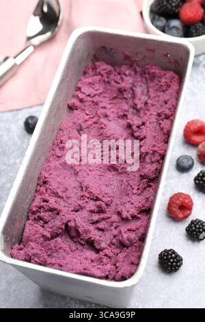 Delicious sorbet in metal container, fresh berries and spoon on grey ...