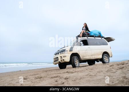 Portrait of happy female traveler sitting on suitcase with cell phone ...