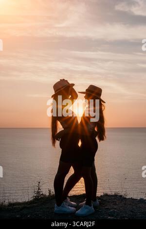 Silhouettes of Two Women in Hats on a Cliffside at Sunset Stock Photo ...