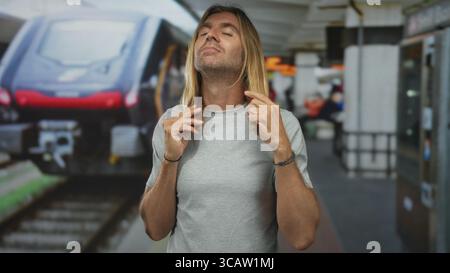 Blond man runs fingers through hair on train station platform by ...