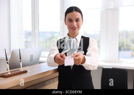 Smiling receptionist in uniform giving hotel key card to guest at ...