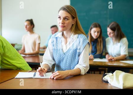 Portrait of female student writing lectures in workbooks in classroom ...