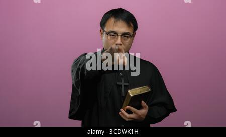 Priest holding bible pointing forward against pink background ...