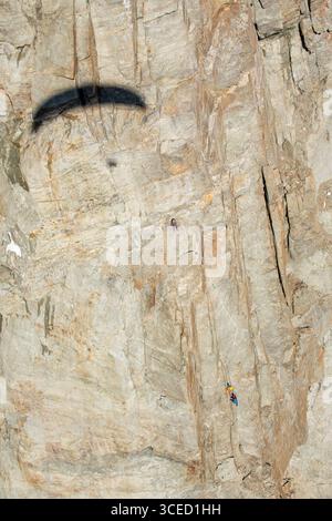 Rock climbers scaling a rugged cliff face with trees and cloudy sky in ...