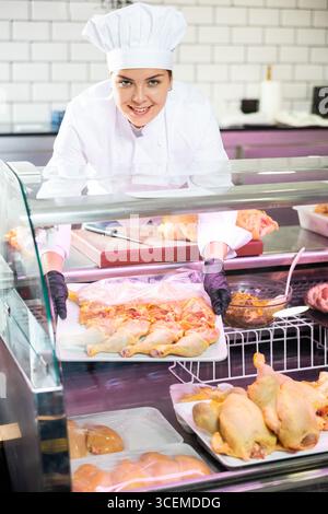 Happy female butcher holding whole chicken in meat section of ...