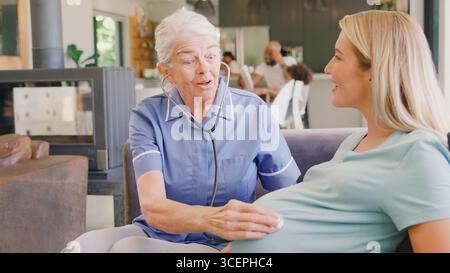 Senior Midwife With Stethoscope Visiting Pregnant Woman At Home With ...