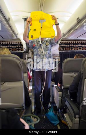 A flight attendant demonstrating life vest to passengers in an airplane ...
