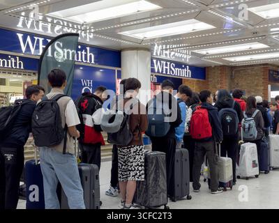 A long line of travellers with suitcases is seen outside a WHSmith shop ...