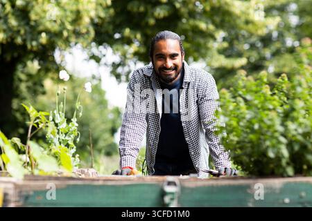 A person tends to a lush, green garden in front of a rustic stone ...