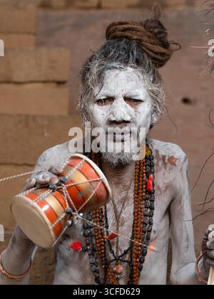 A Hindu Holy man, with ash smeared on his body, tries to stretch as he ...