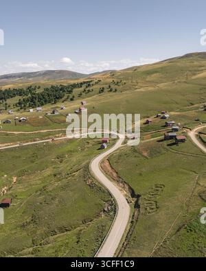 Aerial view of small rural asphalt road located on grassy lush terrain ...