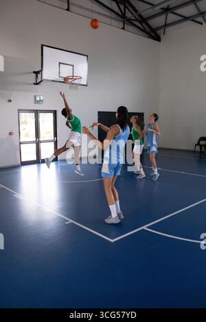 Diverse female opponents jumping and reaching for orange basketball ...