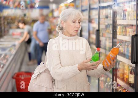 Female customer choosing soft drinks in grocery store, looking at ...