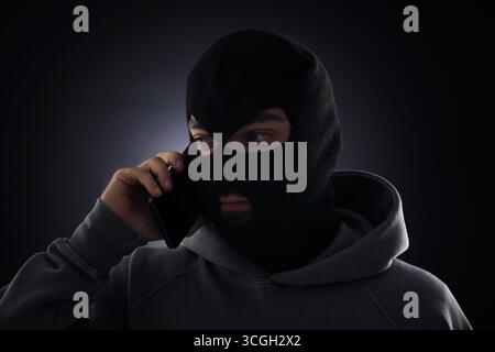 Criminal in mask talking on phone against dark background Stock Photo ...